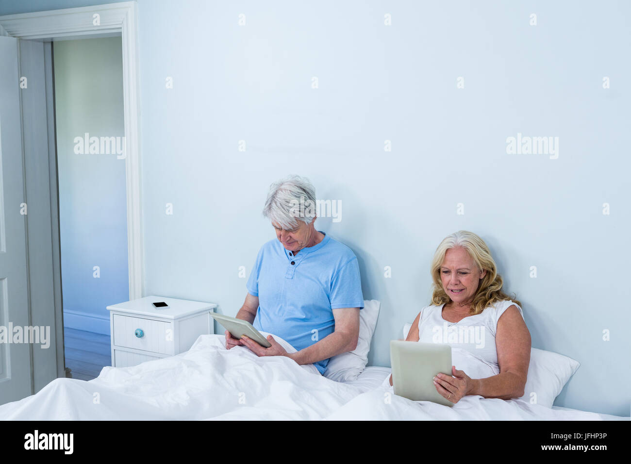 Retired couple using digital tablets while sitting on bed Stock Photo ...
