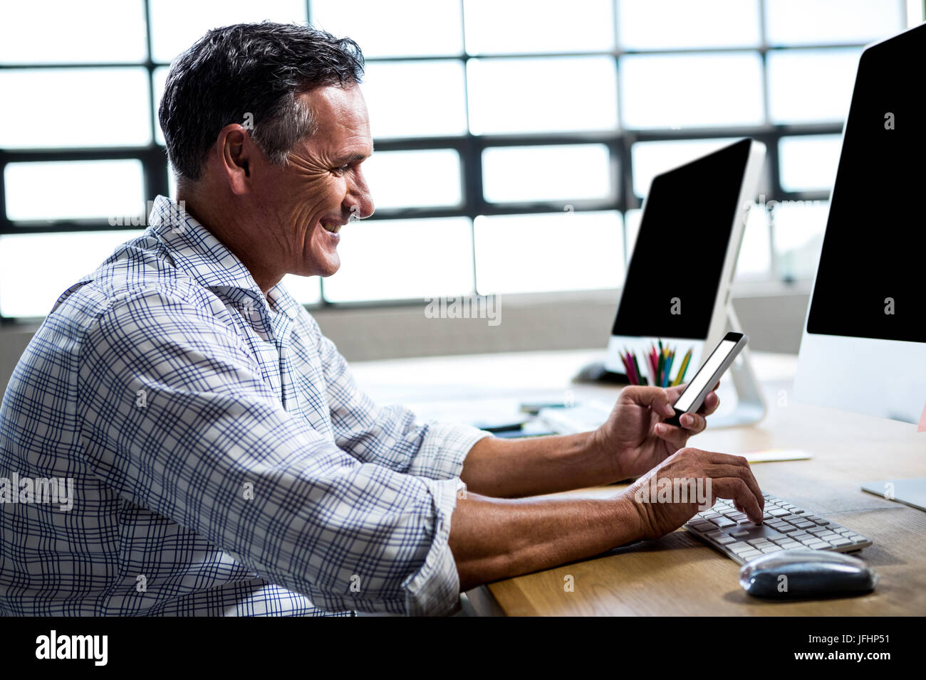Man text messaging on mobile phone while using computer Stock Photo - Alamy