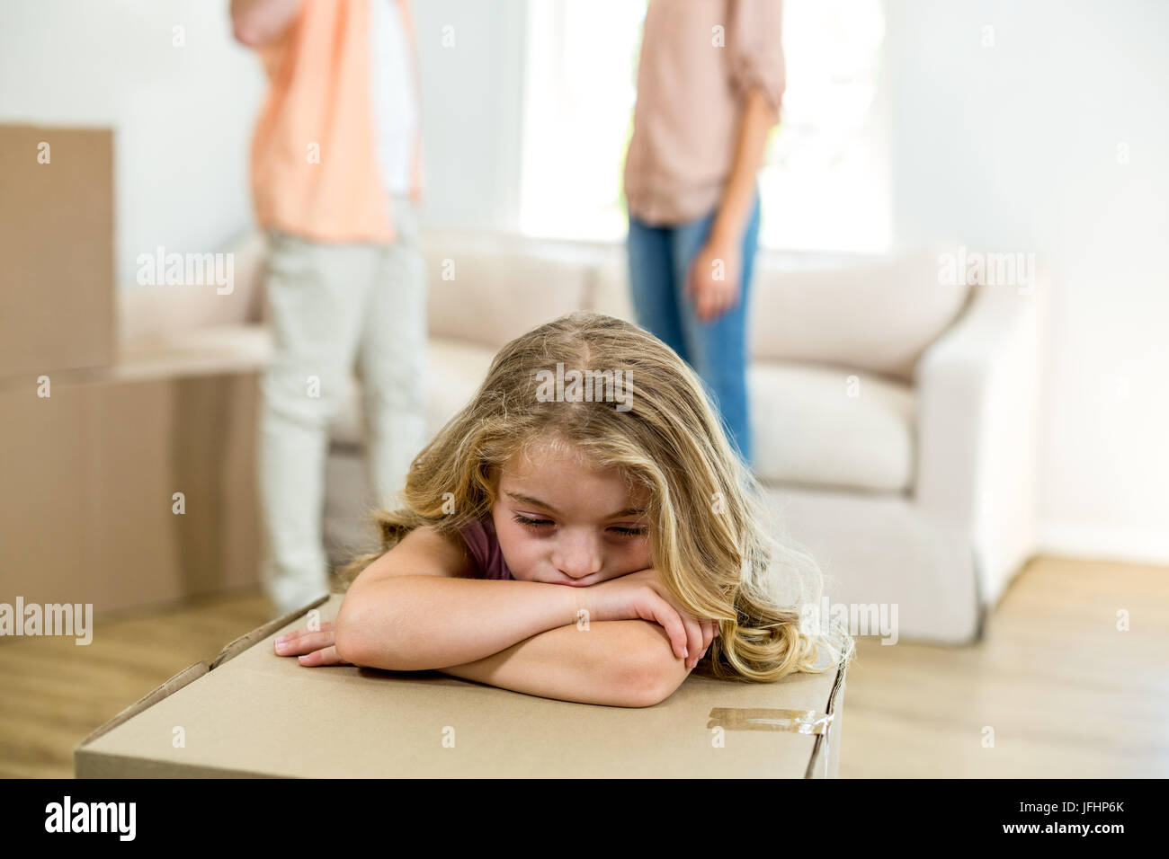 upset girl leaning on box while parents in background Stock Photo - Alamy