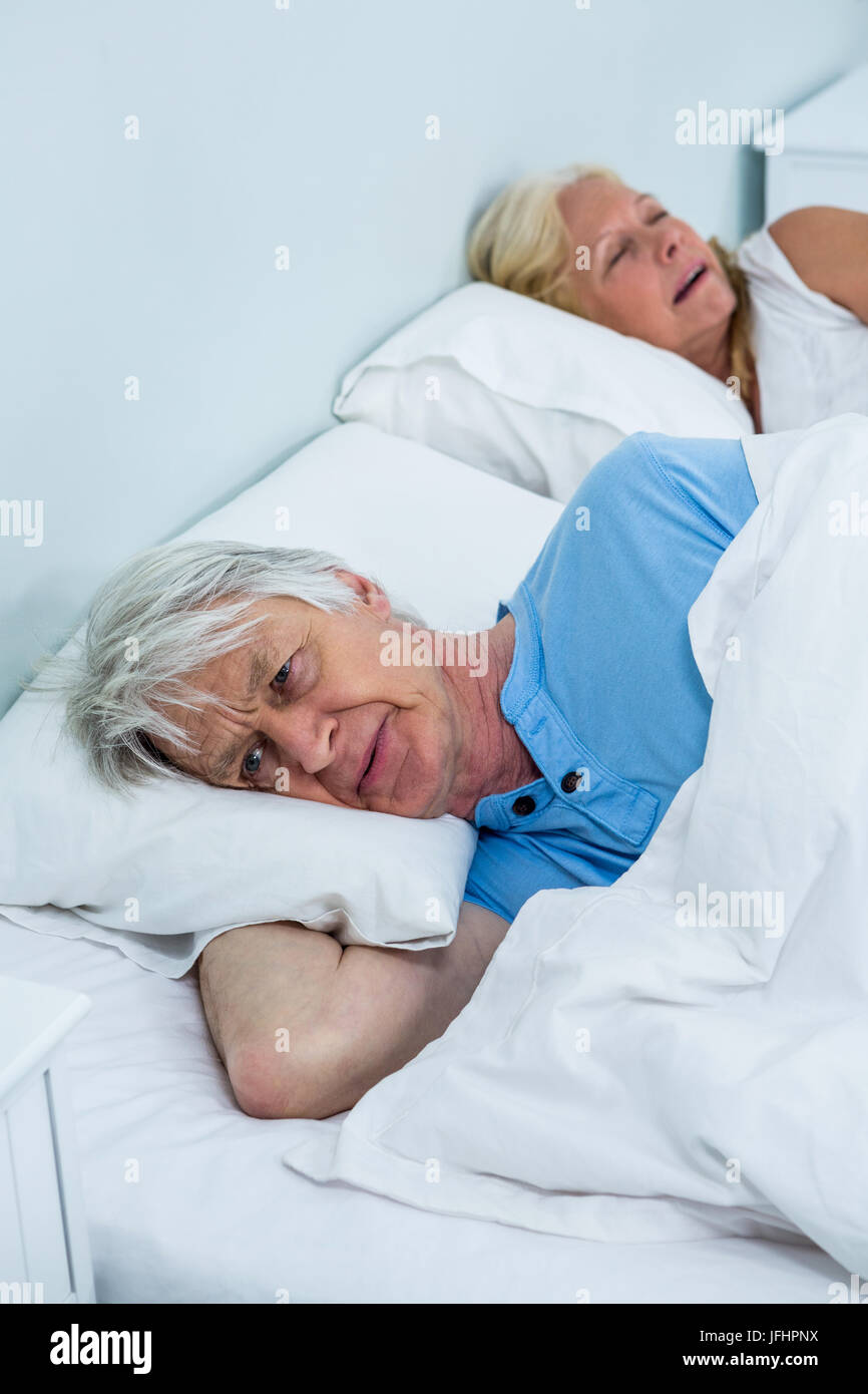 Thoughtful senior man relaxing on bed while woman snoring Stock Photo ...