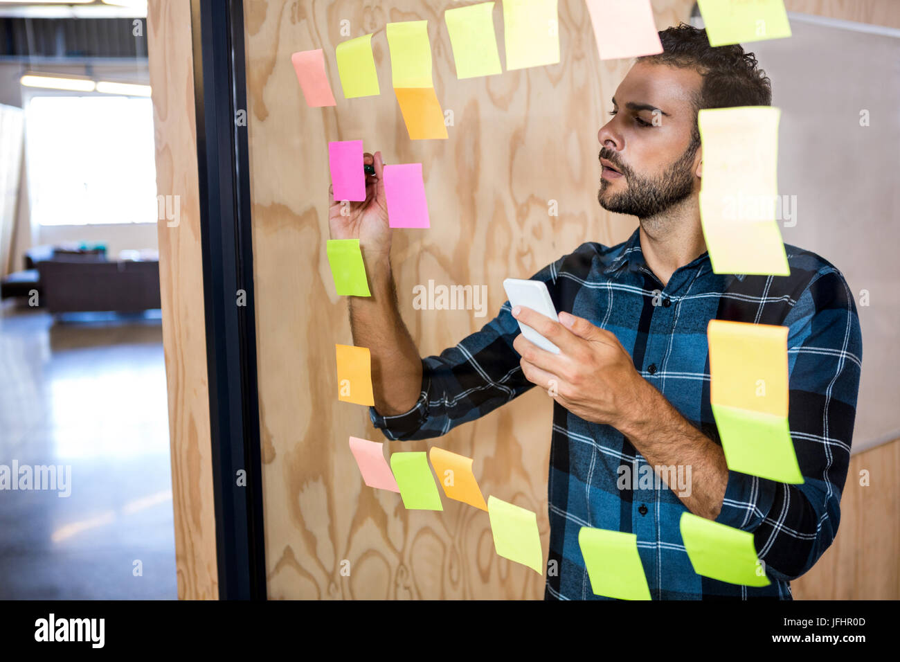 Man using mobile phone while writing on sticky notes Stock Photo - Alamy