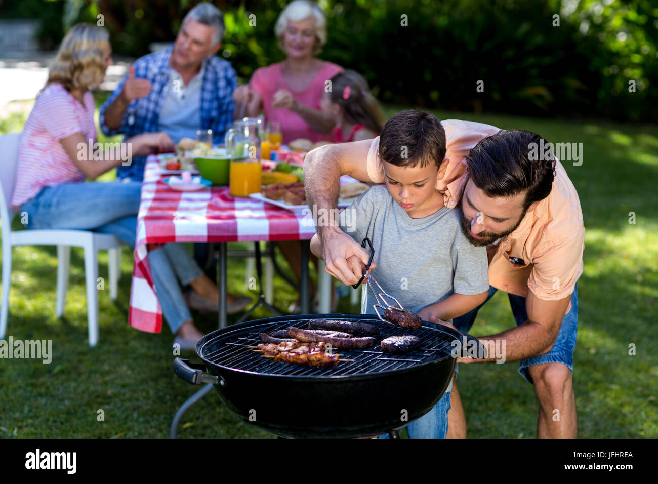 Father teaching son cooking on barbecue with family Stock Photo - Alamy