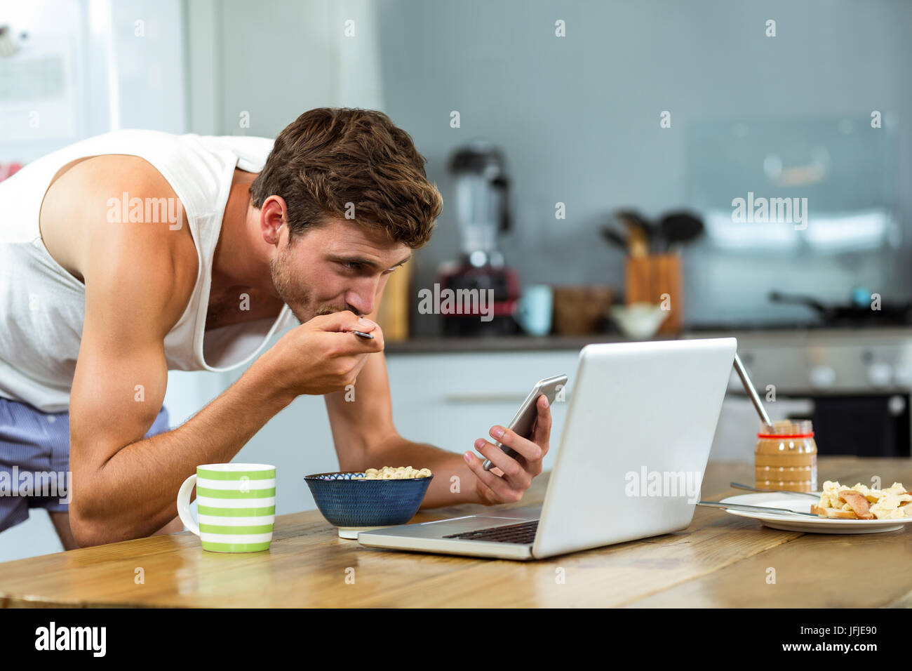 Man having breakfast while using mobile phone in kitchen Stock Photo ...