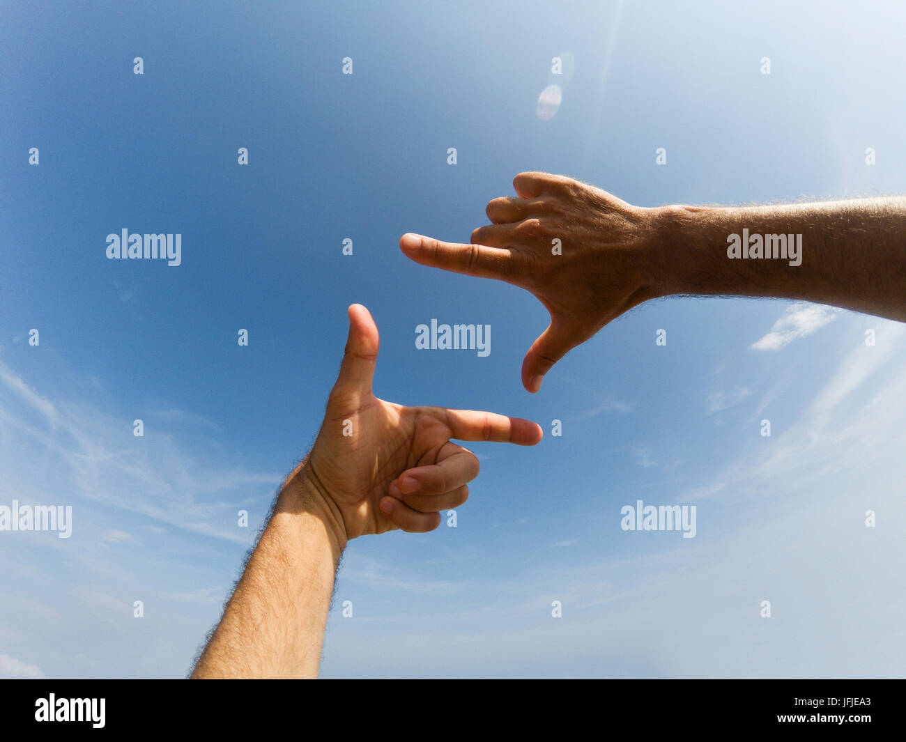 Two hands form with a fingers a frame in front of a blue sky with ...