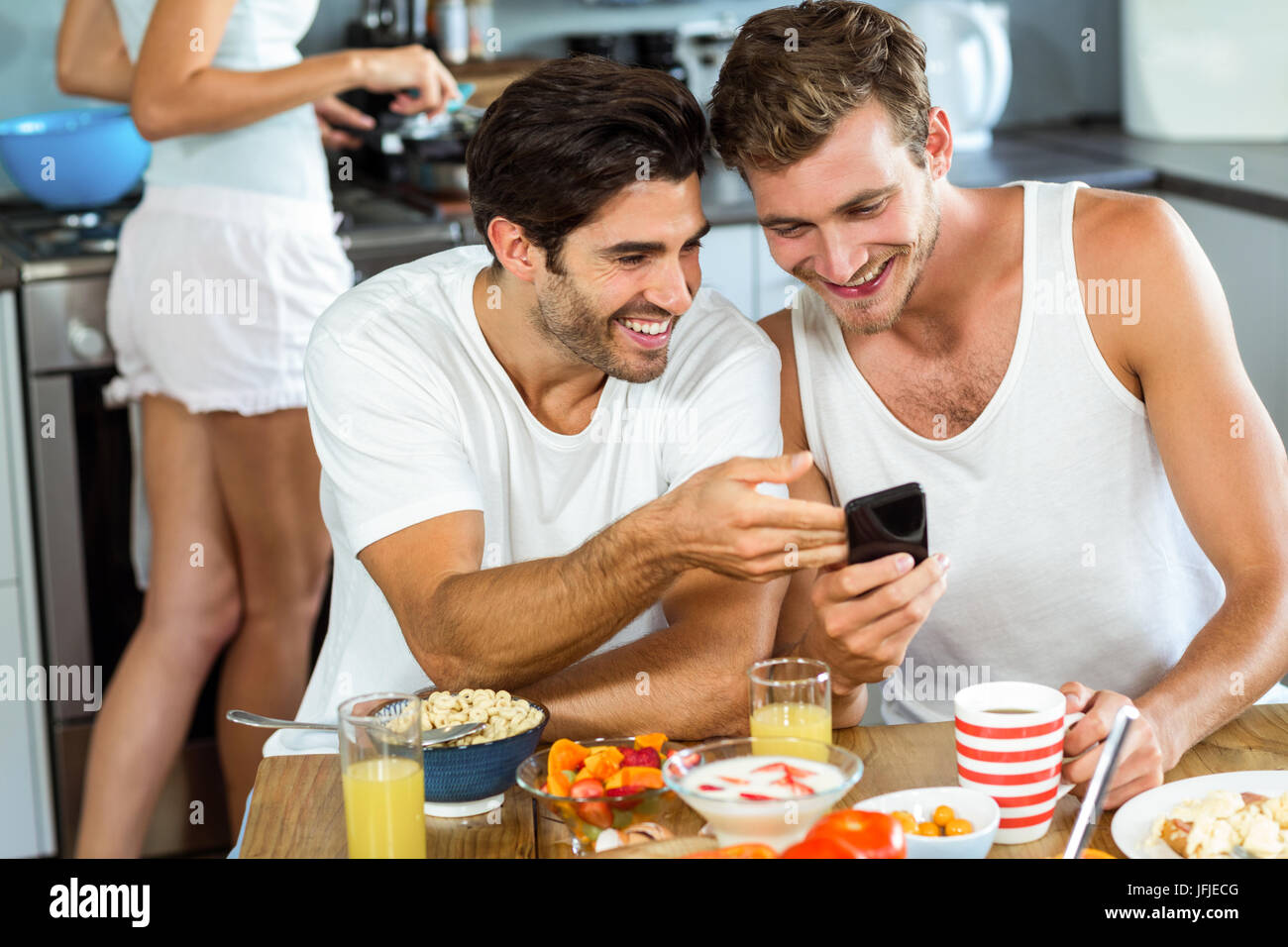 Cheerful men using mobile phone while having breakfast Stock Photo - Alamy