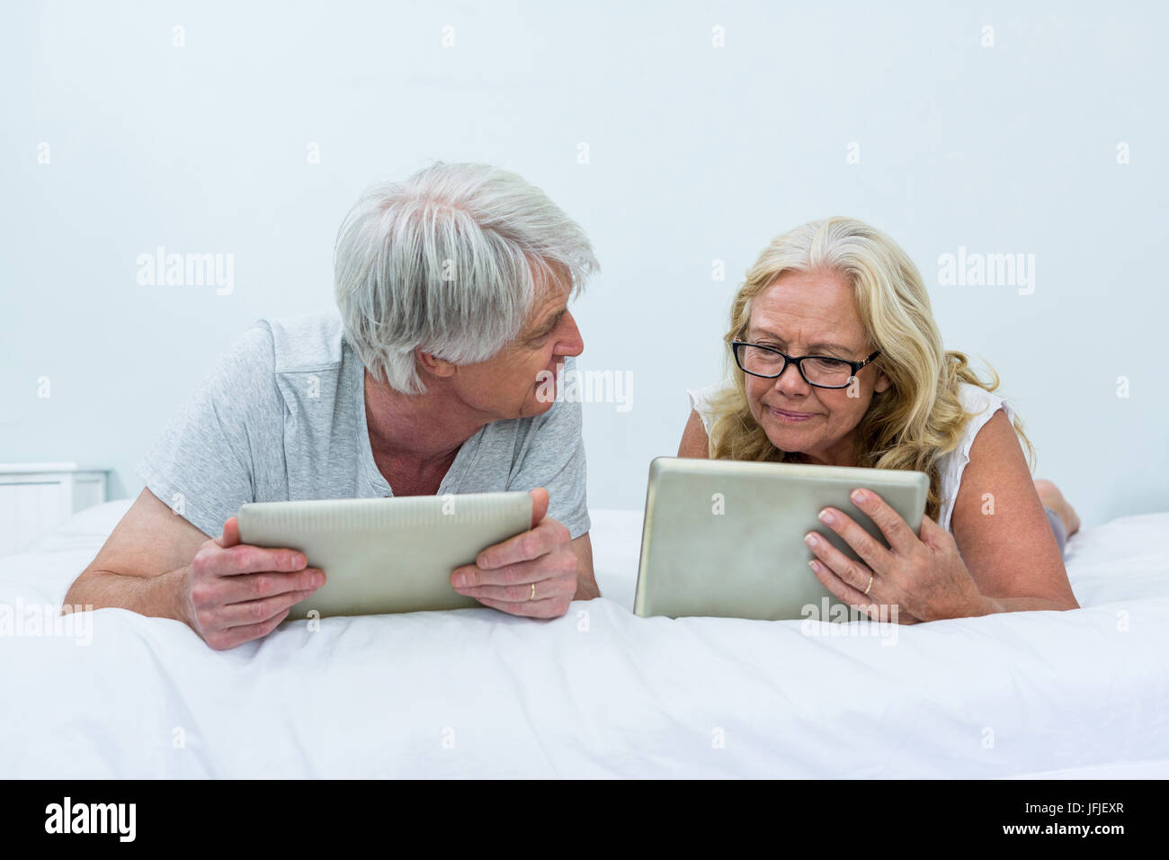 Senior couple talking while using digital tablets on bed Stock Photo - Alamy