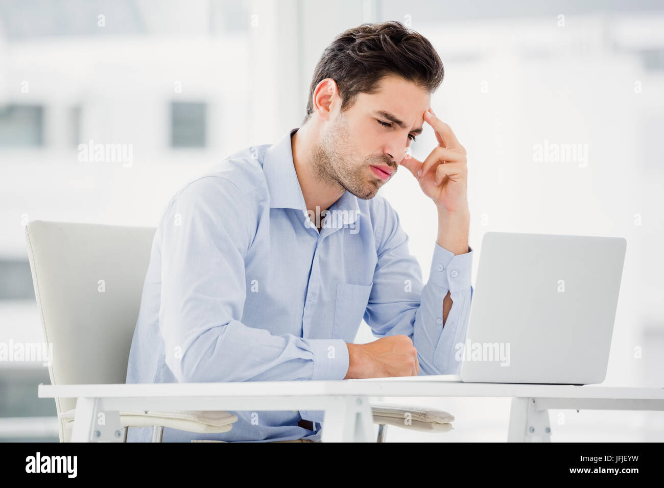 Tensed businessman sitting at table with laptop Stock Photo - Alamy