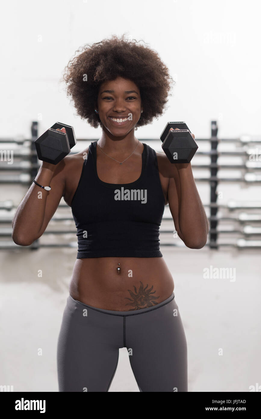 young beautiful African American woman doing bicep curls in a gym Stock ...