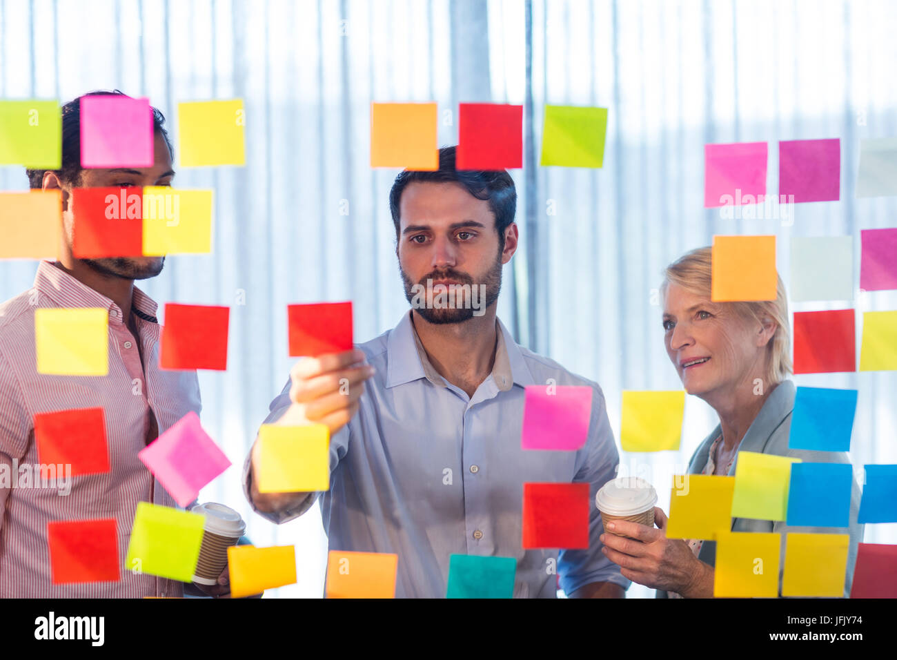 Business people looking at post it on the wall Stock Photo - Alamy