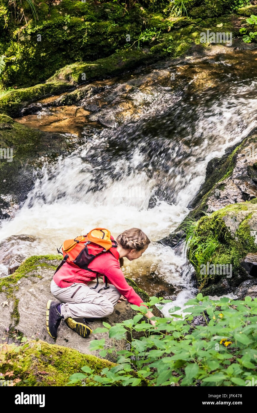 Girl sitting on rocks beside waterfall Stock Photo - Alamy