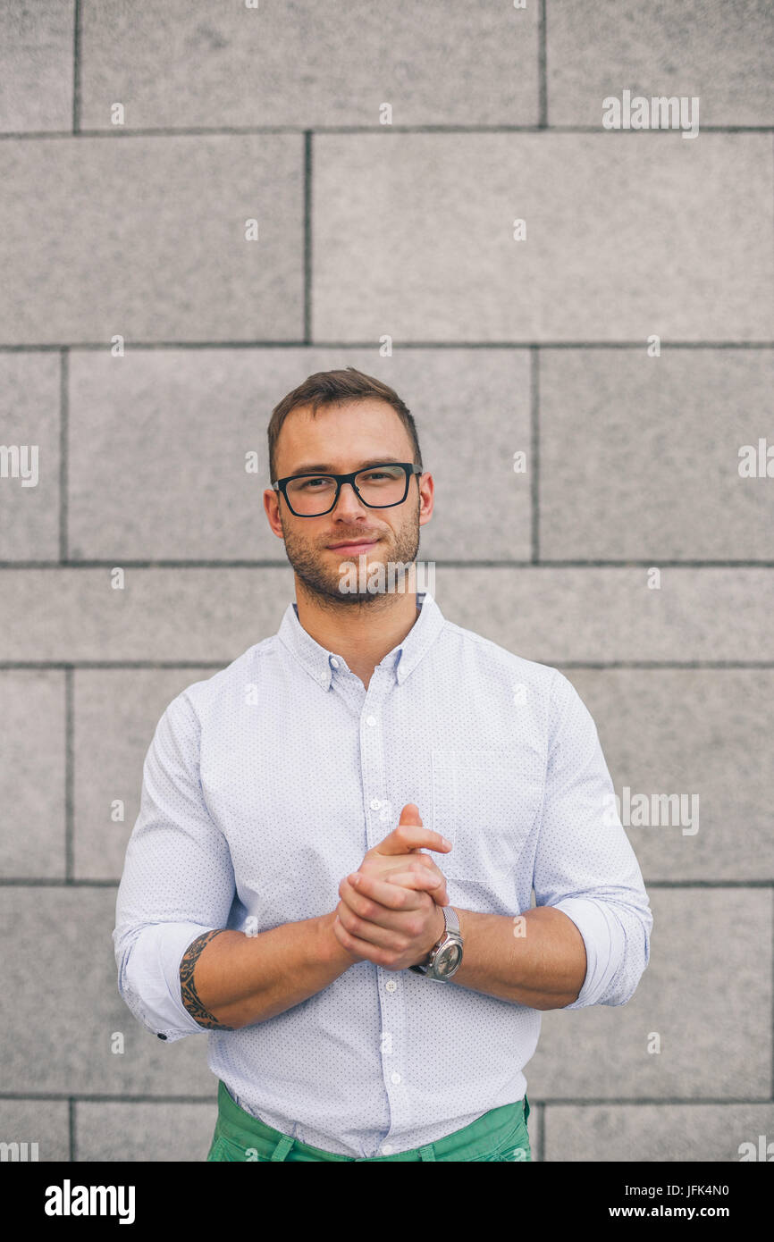 Young handsome man with folded hands standing against concrete wall ...