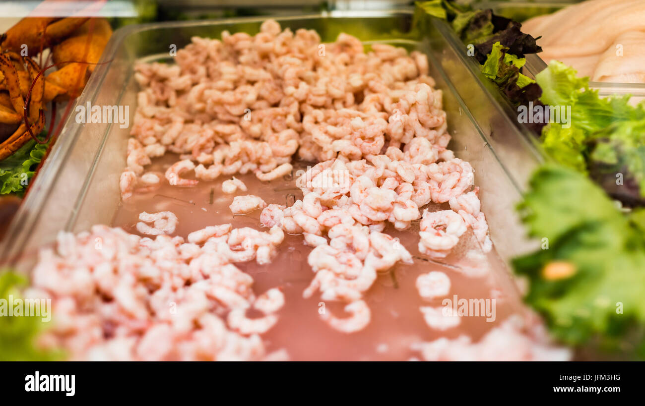 Closeup of many pink small cooked shrimp on display in seafood shop ...
