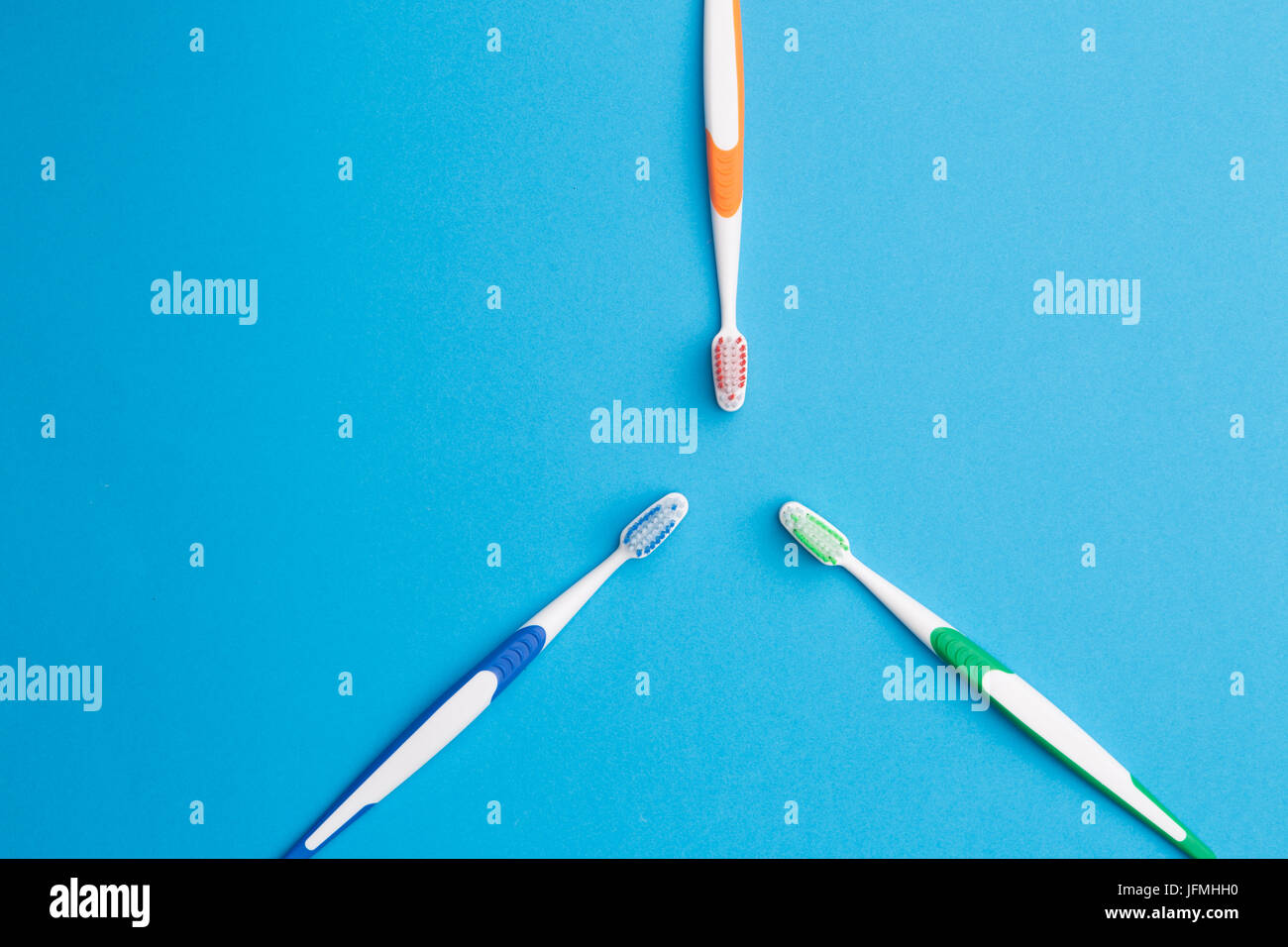 Three multi-colored toothbrushes on empty blue background with place ...