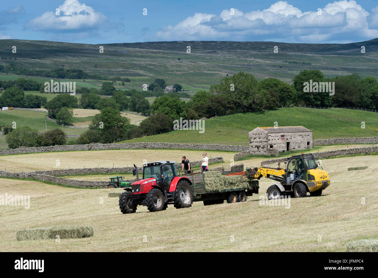 Picking up small bales of hay in upland meadow in Wensleydale, using a ...