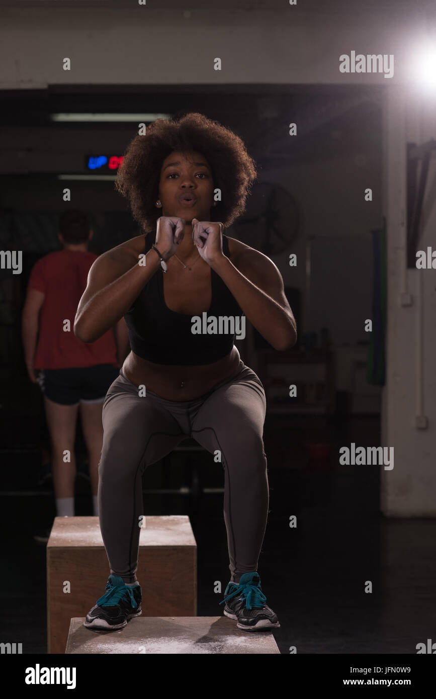 Fit young african american woman box jumping at a crossfit style gym ...