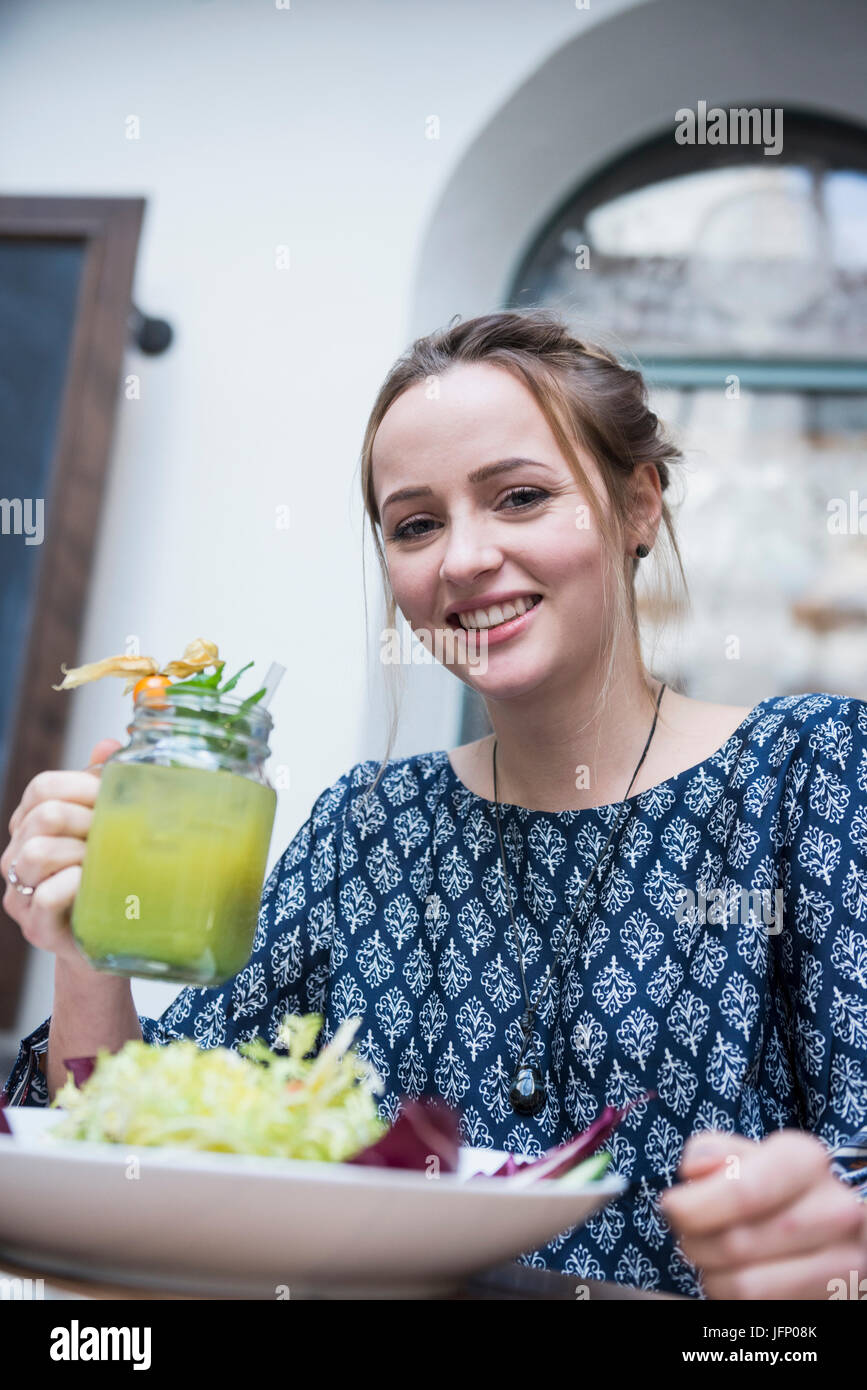 Portrait of young woman holding mocktail in jar glass by salad bowl ...