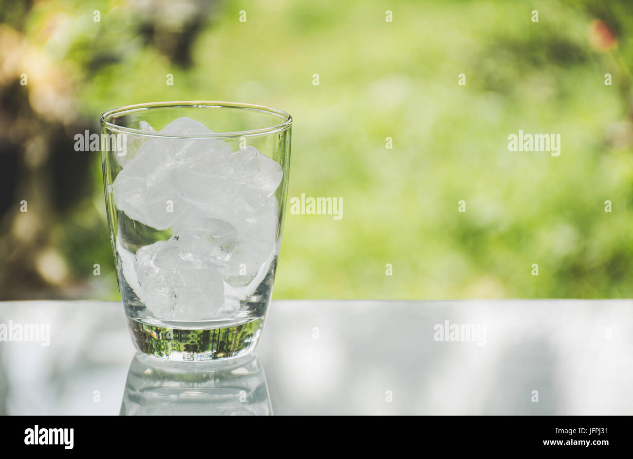 Ice cube in the glass on table with nature background Stock Photo - Alamy