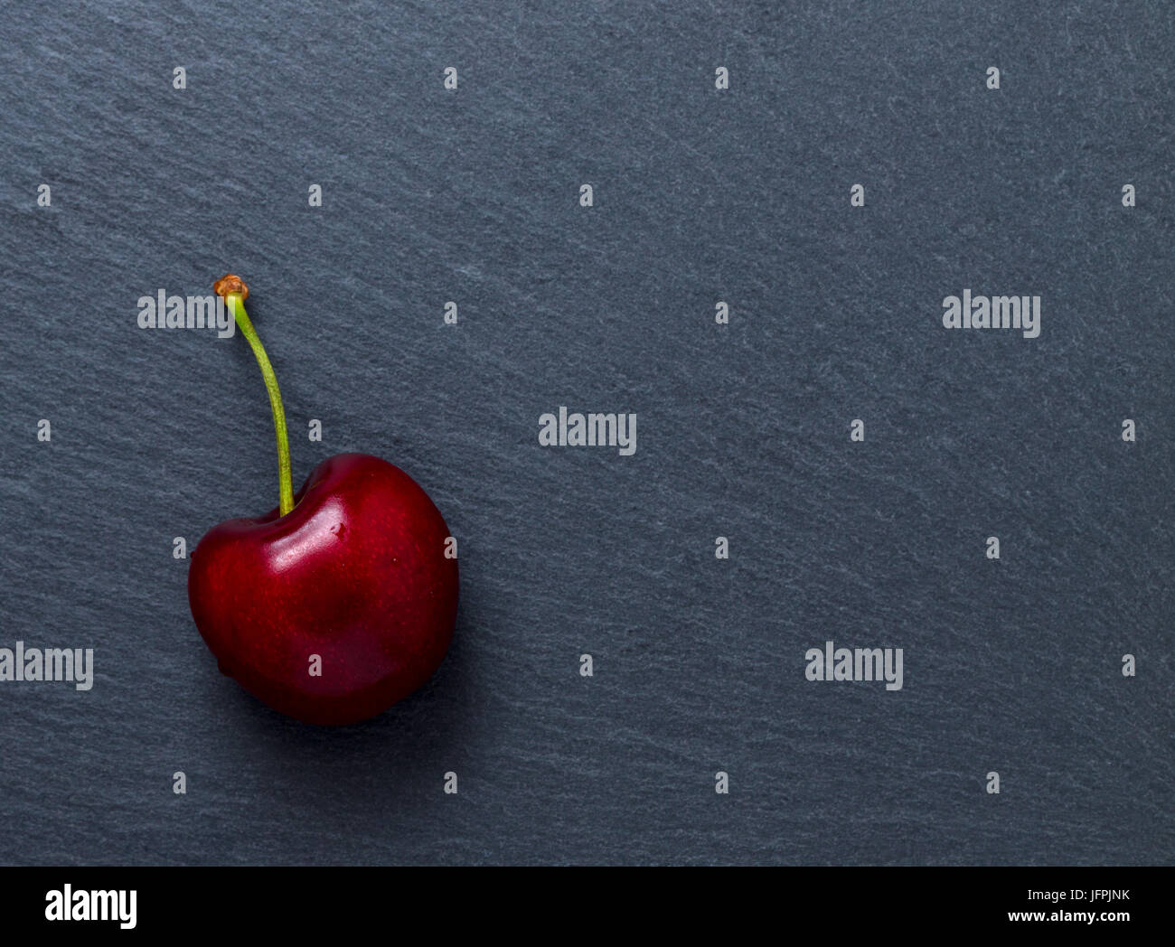 one cherry isolated on a grey slate Stock Photo - Alamy