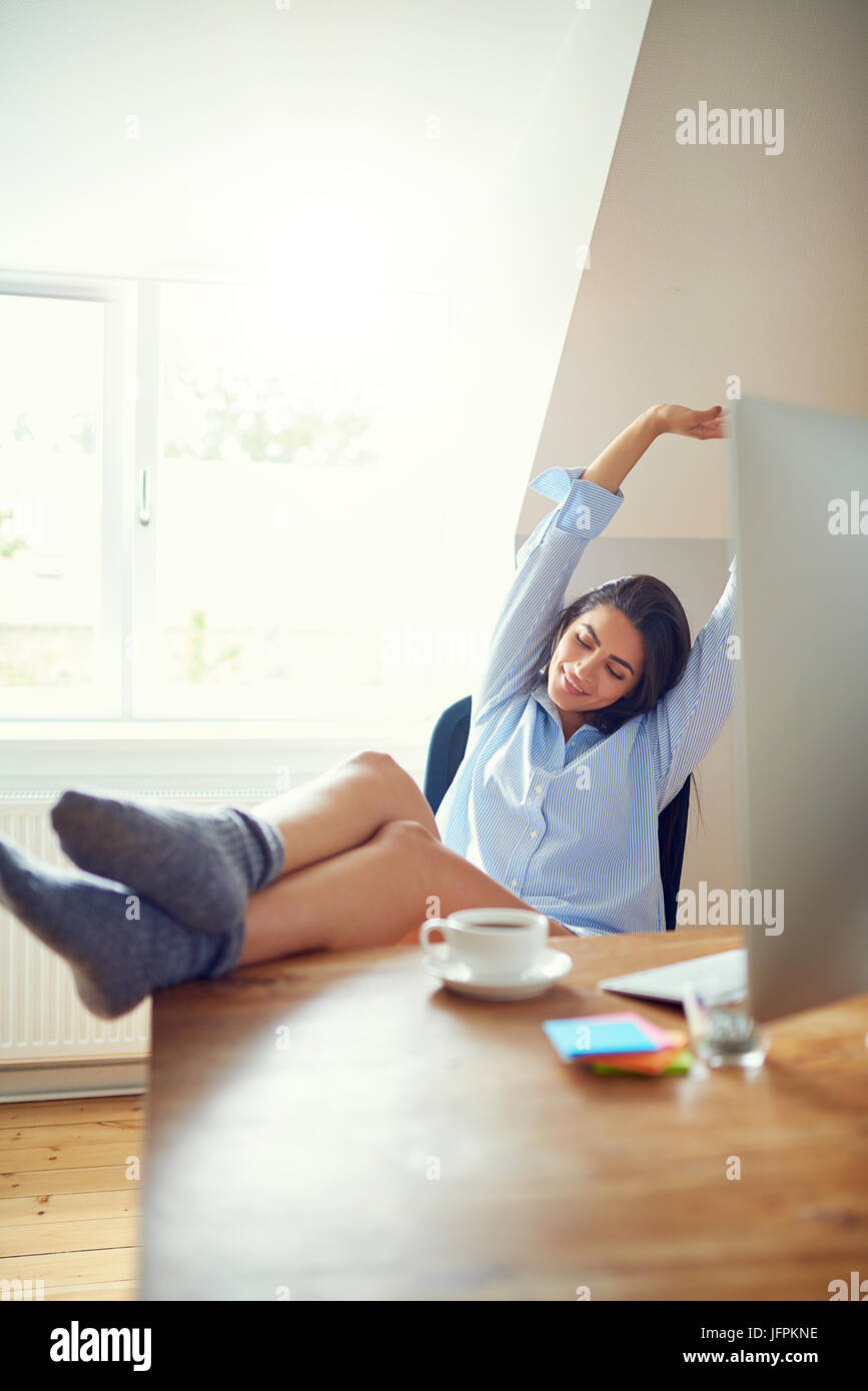 Stretching young woman with tired expression and feet on desk at home ...