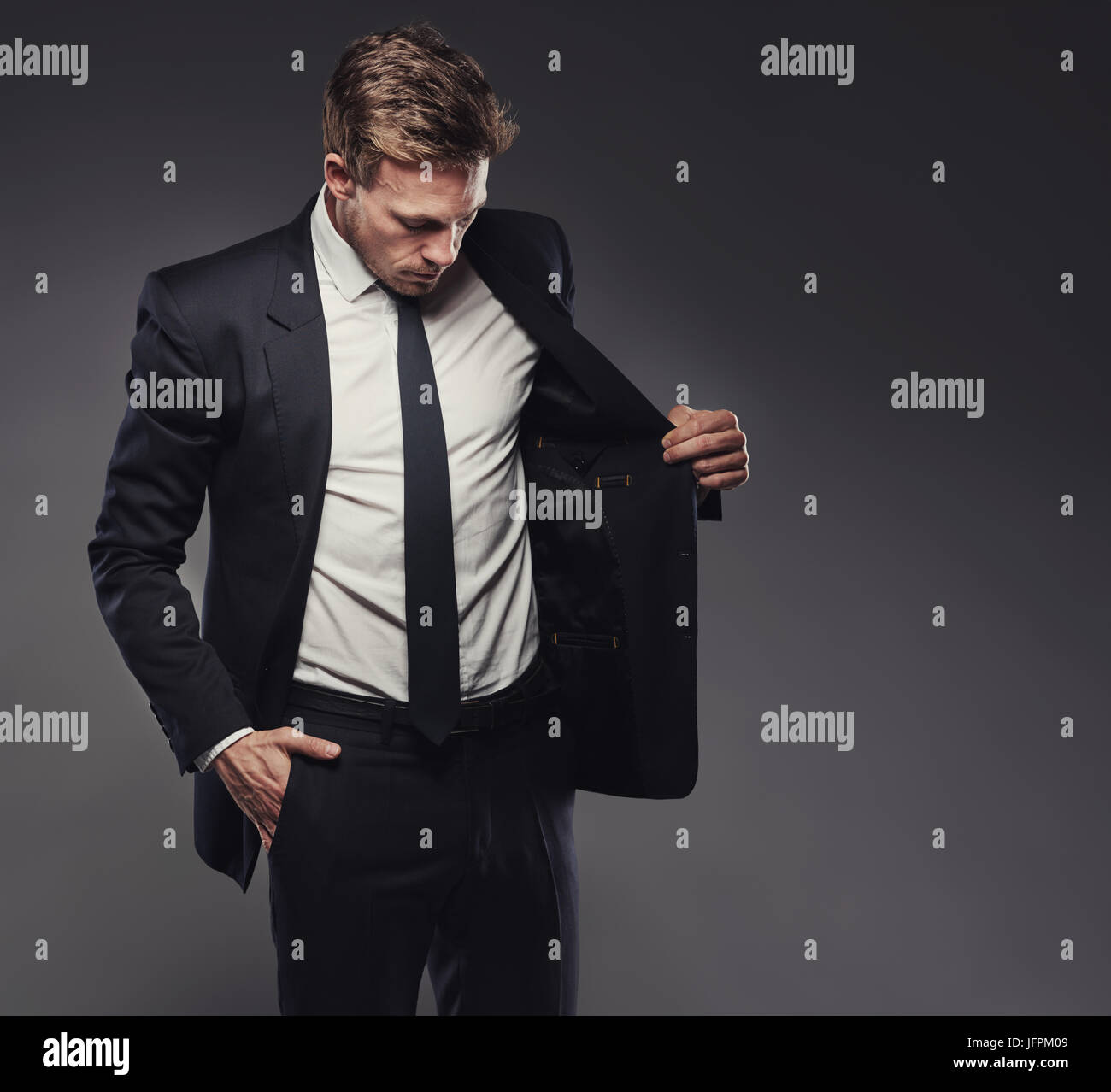 Suave young businessman checking out the jacket of a stylish black suit ...