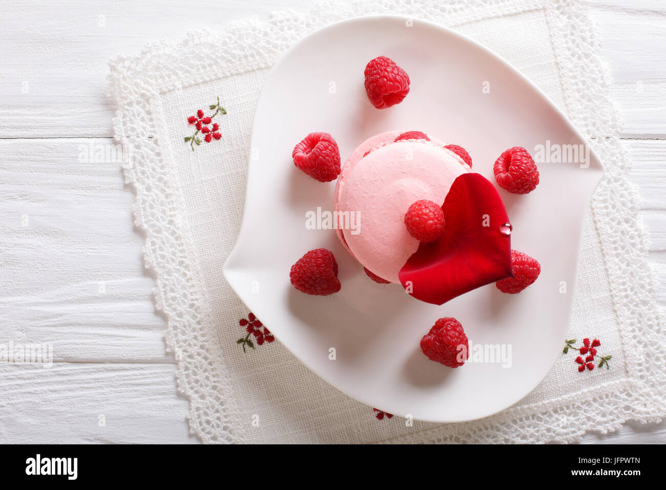 Pink macaroon with fresh raspberries and rose close-up on a plate ...