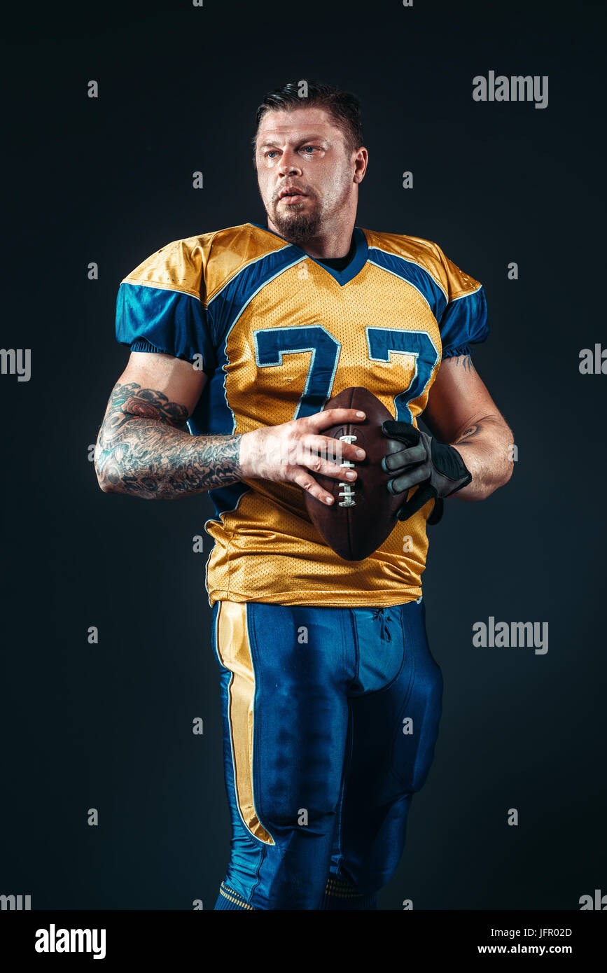 American football player poses with ball in hands, black background ...