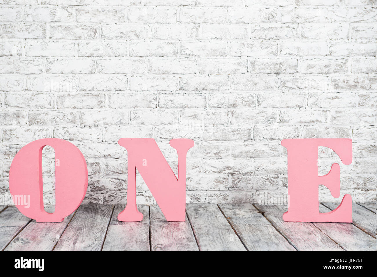 Large pink letters ONE against a white brick wall Stock Photo - Alamy