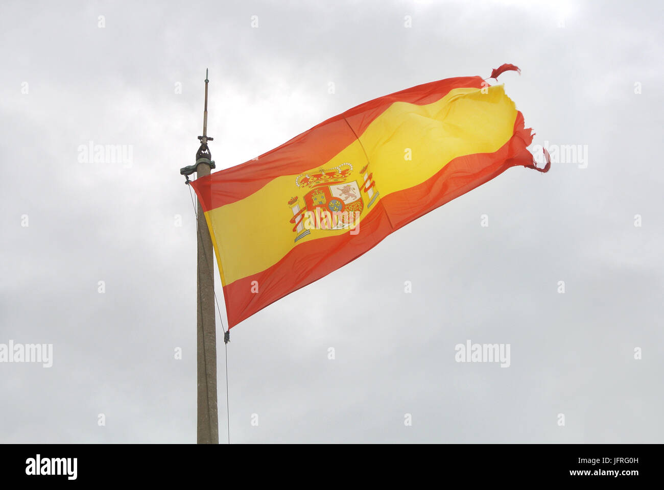 Old Spanish flag on a pole, undulating in the wind with clouds at the ...