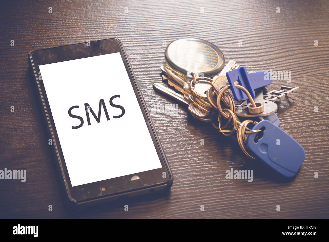 sms on mobile screen with view of keys on wooden table in office Stock ...