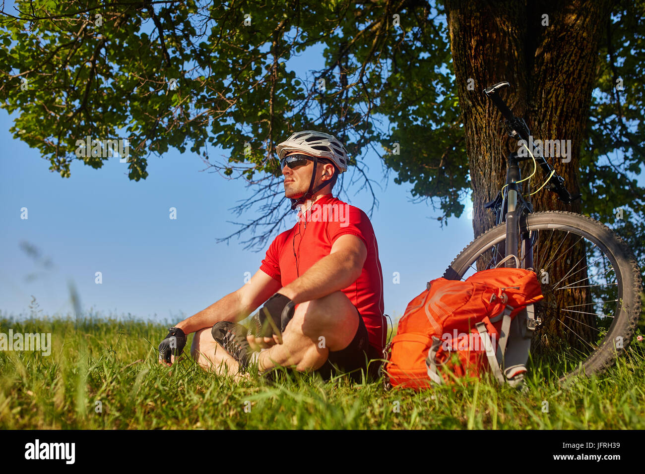 Traveler cyclist have a rest under oak tree with his bike behind him on ...