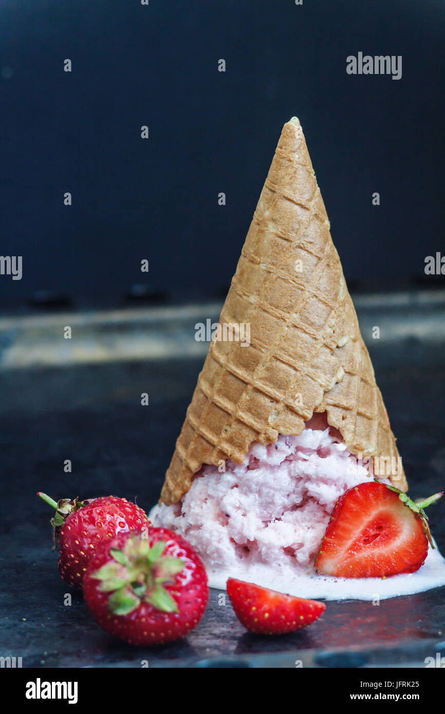 Strawberry ice cream in a waffle cone inverted and melted against a ...