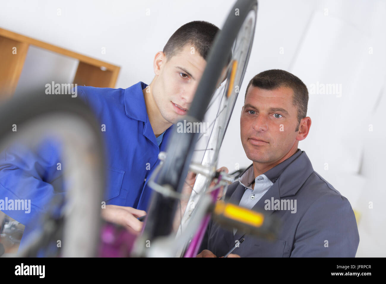 young trainee mechanic repairing bicycle wheel with his teacher Stock ...