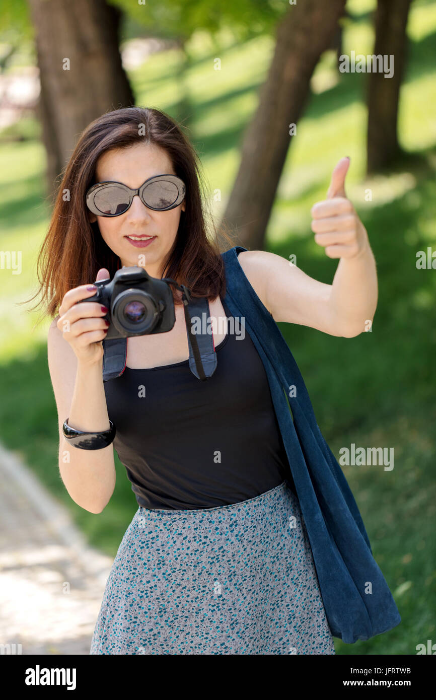 Young woman (photographer, tourist) holds a camera and shows a thumb ...