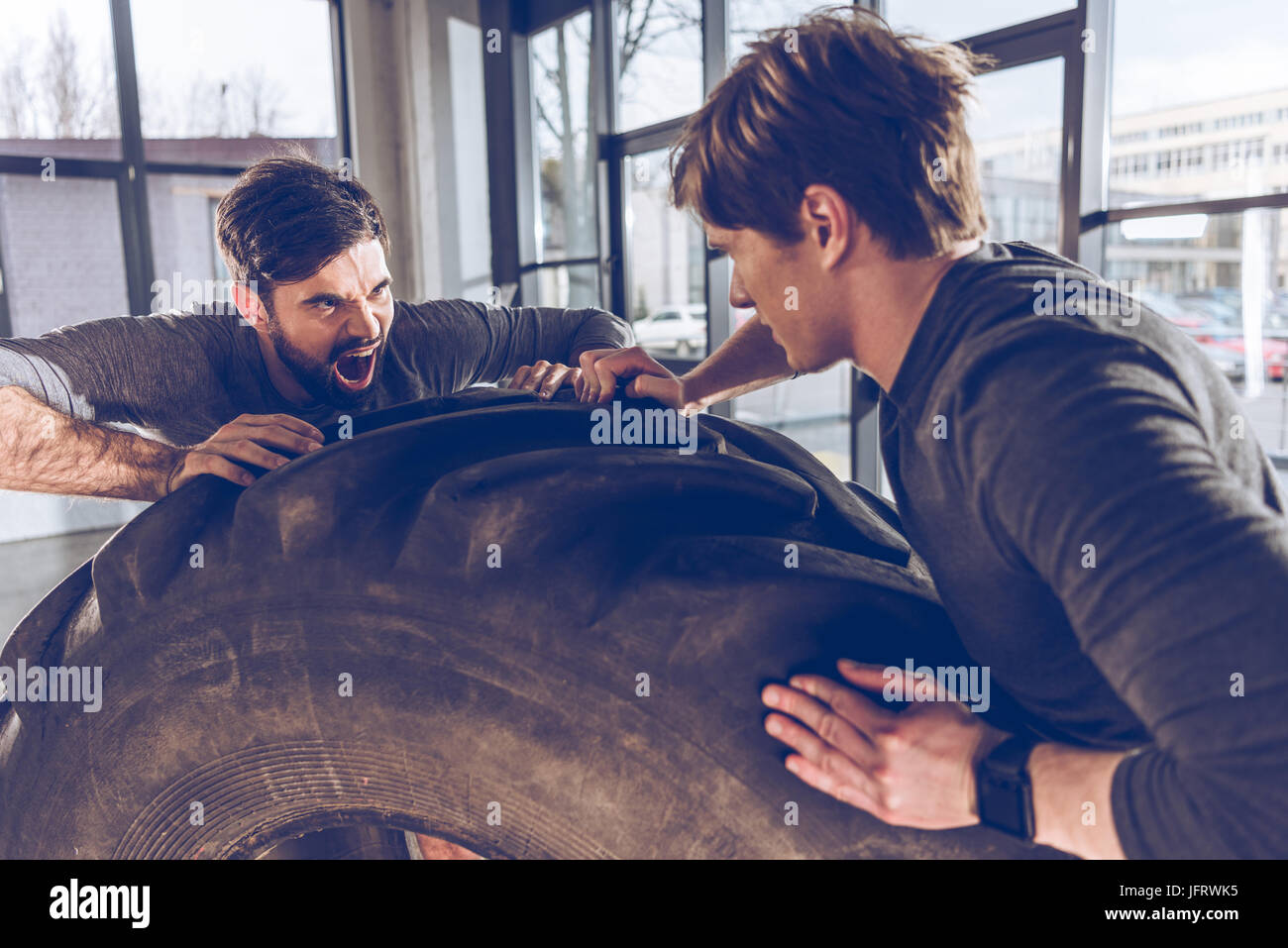 side view of men pulling tire together while exercising at the gym ...