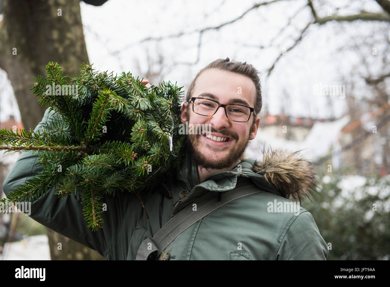 Portrait of young man carrying christmas tree Stock Photo - Alamy