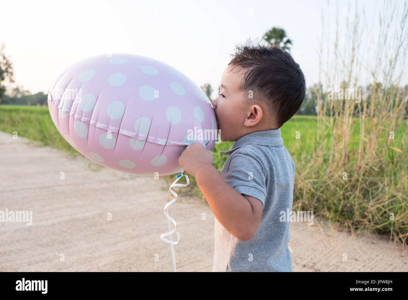 Little boy with a blue dot balloons looking at the in spring field ...