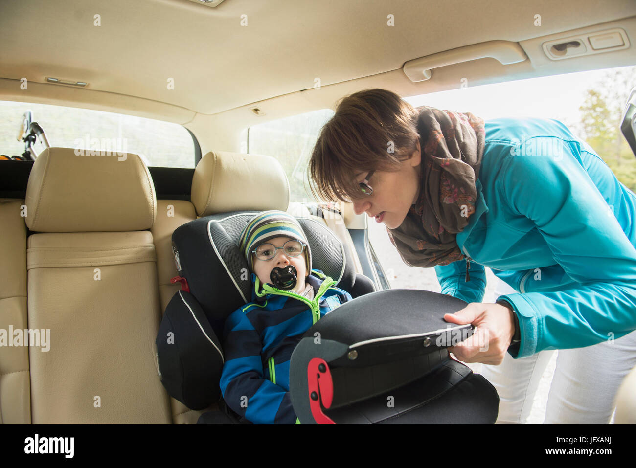 Mother clipping on the seat belt of her son with pacifier in his mouth ...