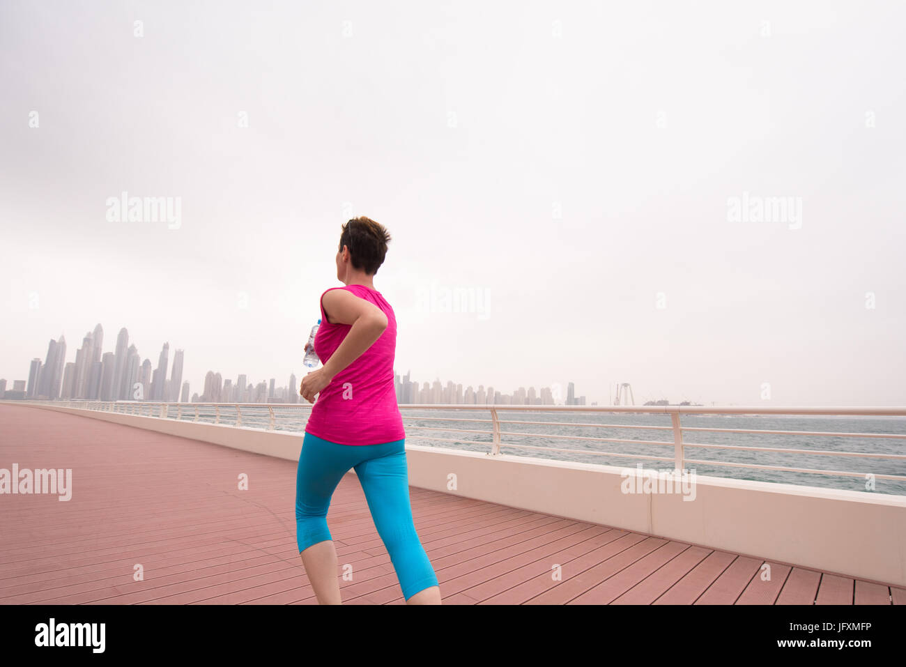 very active young beautiful woman busy running on the promenade along ...