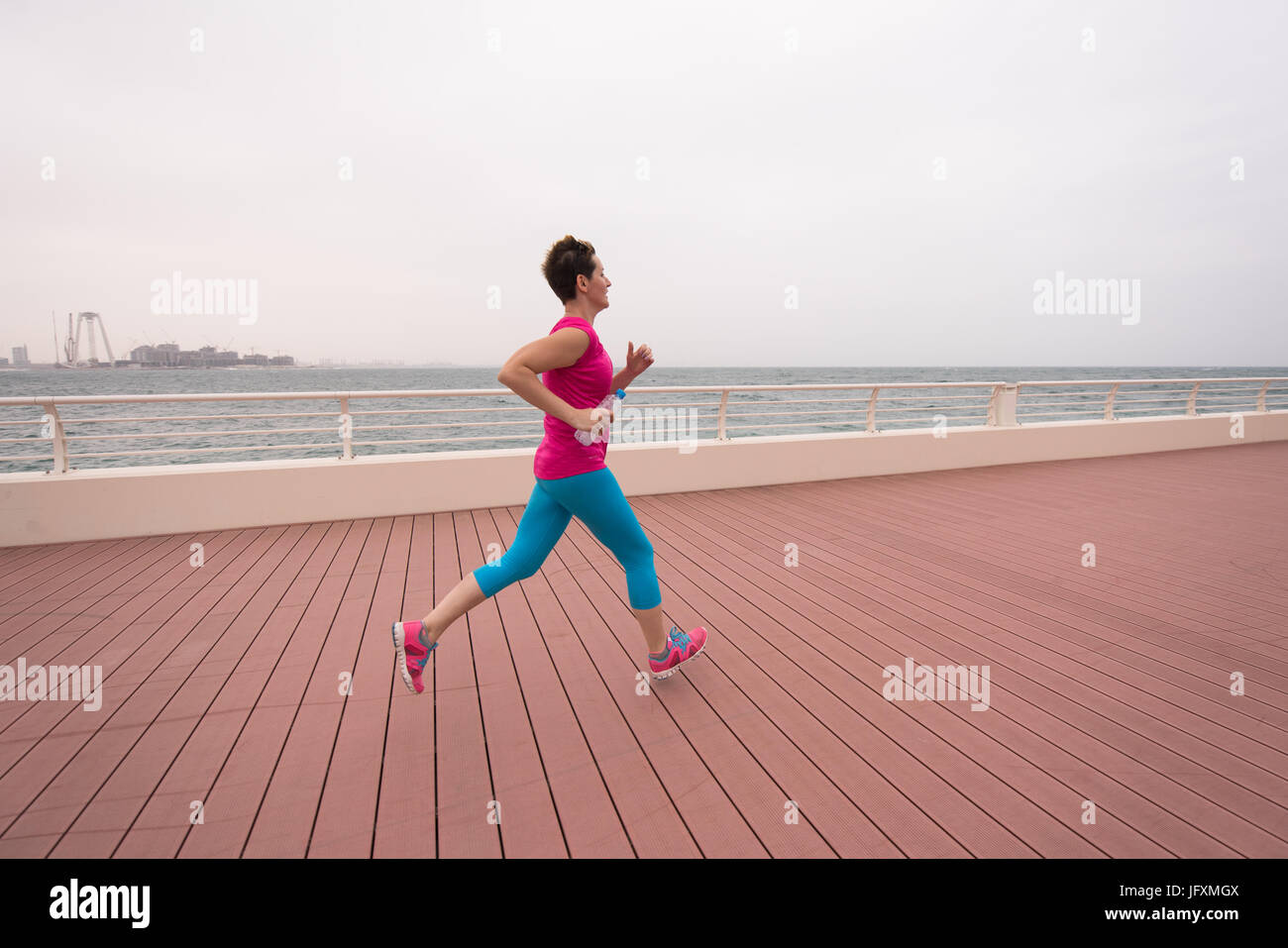 very active young beautiful woman busy running on the promenade along ...