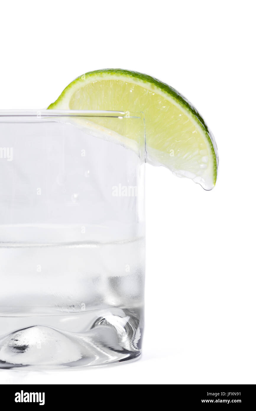 close up of a short glass with a clear liquid and a green lime on the ...