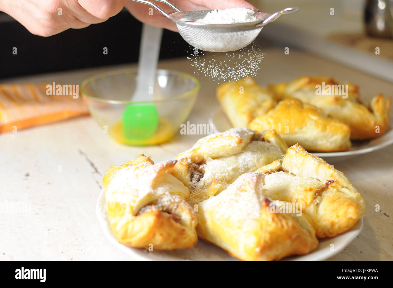 Female hands sprinkle powdered sugar on apple puffs. Process of cooking ...