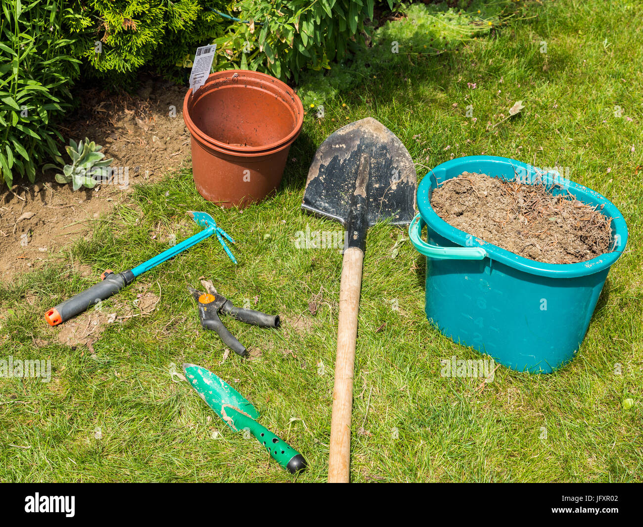 Garden tools lying on grass with bin full of soil Stock Photo - Alamy