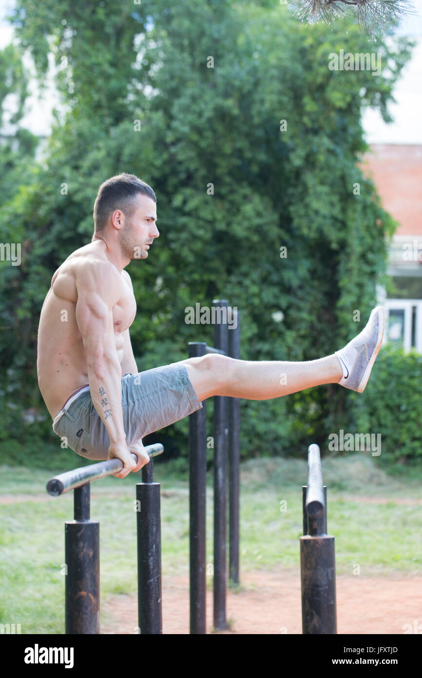 Young muscular man with a perfect body doing exercises on the parallel ...