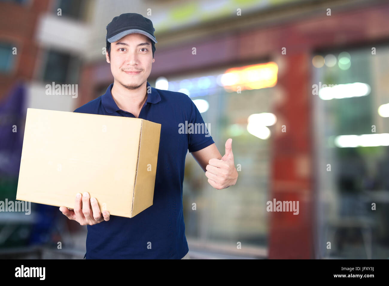 Asian smile Delivery man thumbs up with cardboard box in hand standing ...