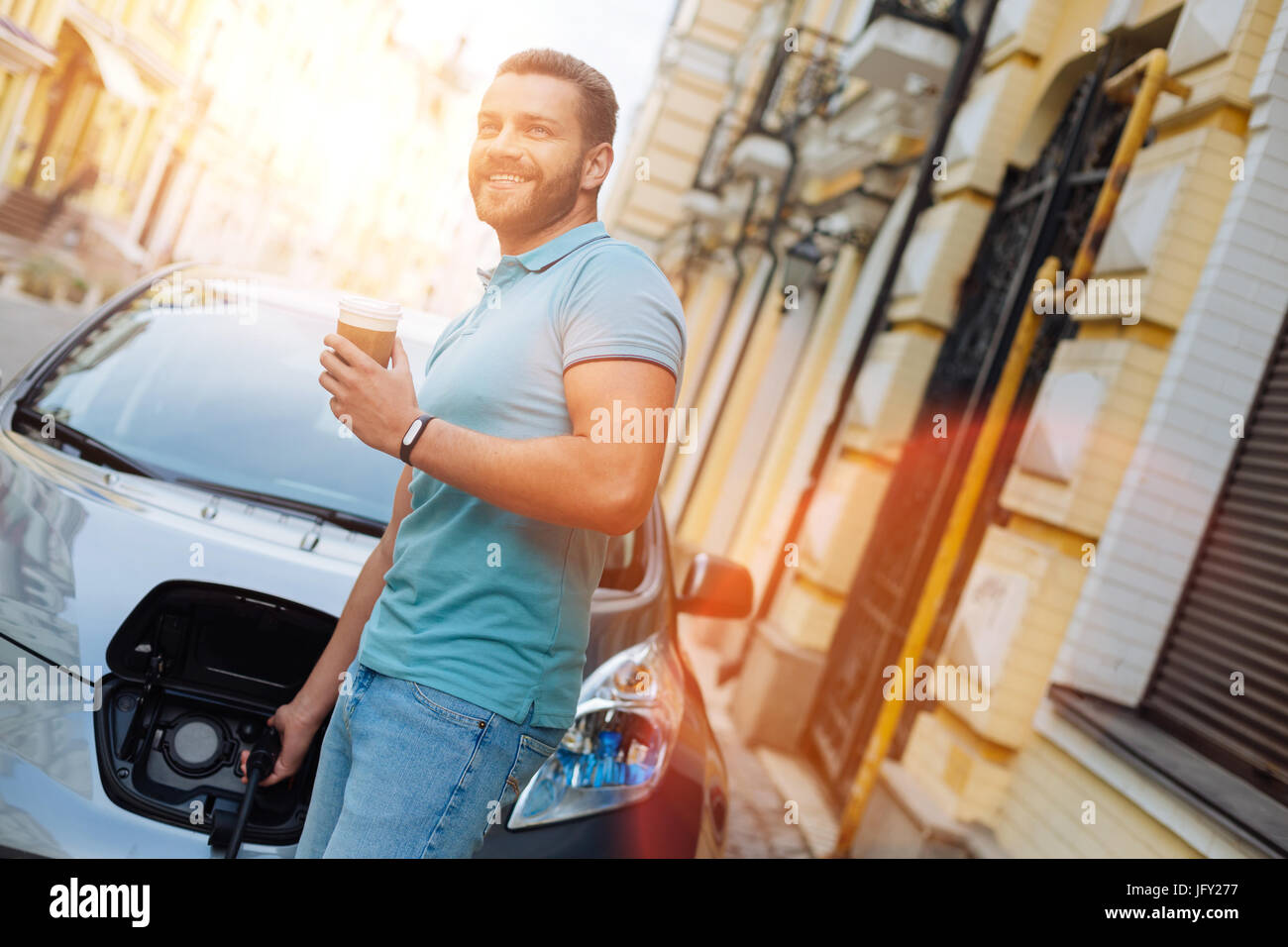 Young man charging his car and drinking coffee Stock Photo - Alamy