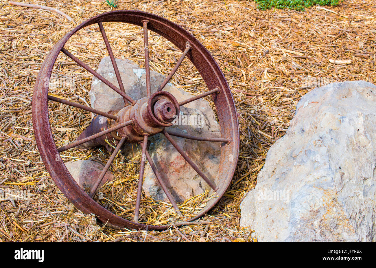 weathered rusting wagon wheel against rock on ground Stock Photo - Alamy