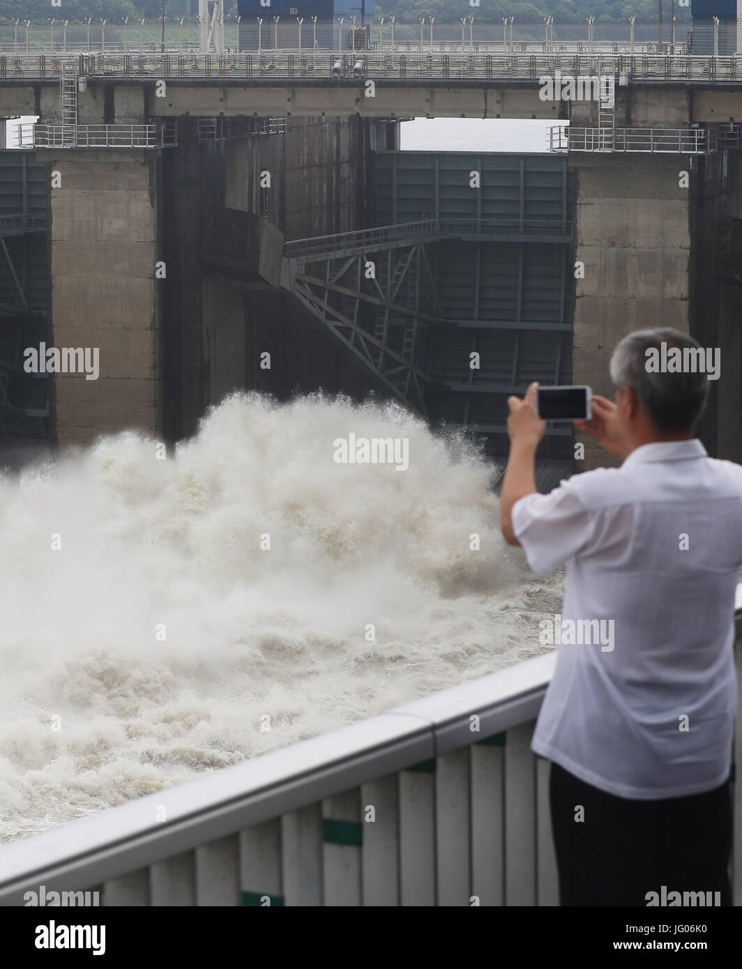 Rainy season A man photographs water pouring out of floodgates at ...