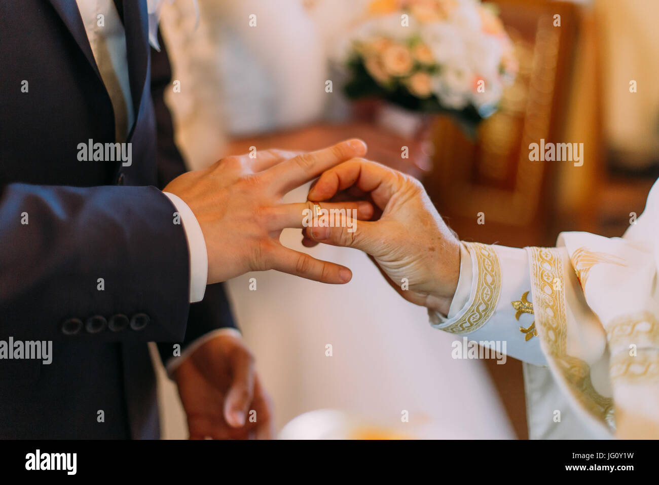 The horizontal close-up view of the priest putting on the groom golden ...