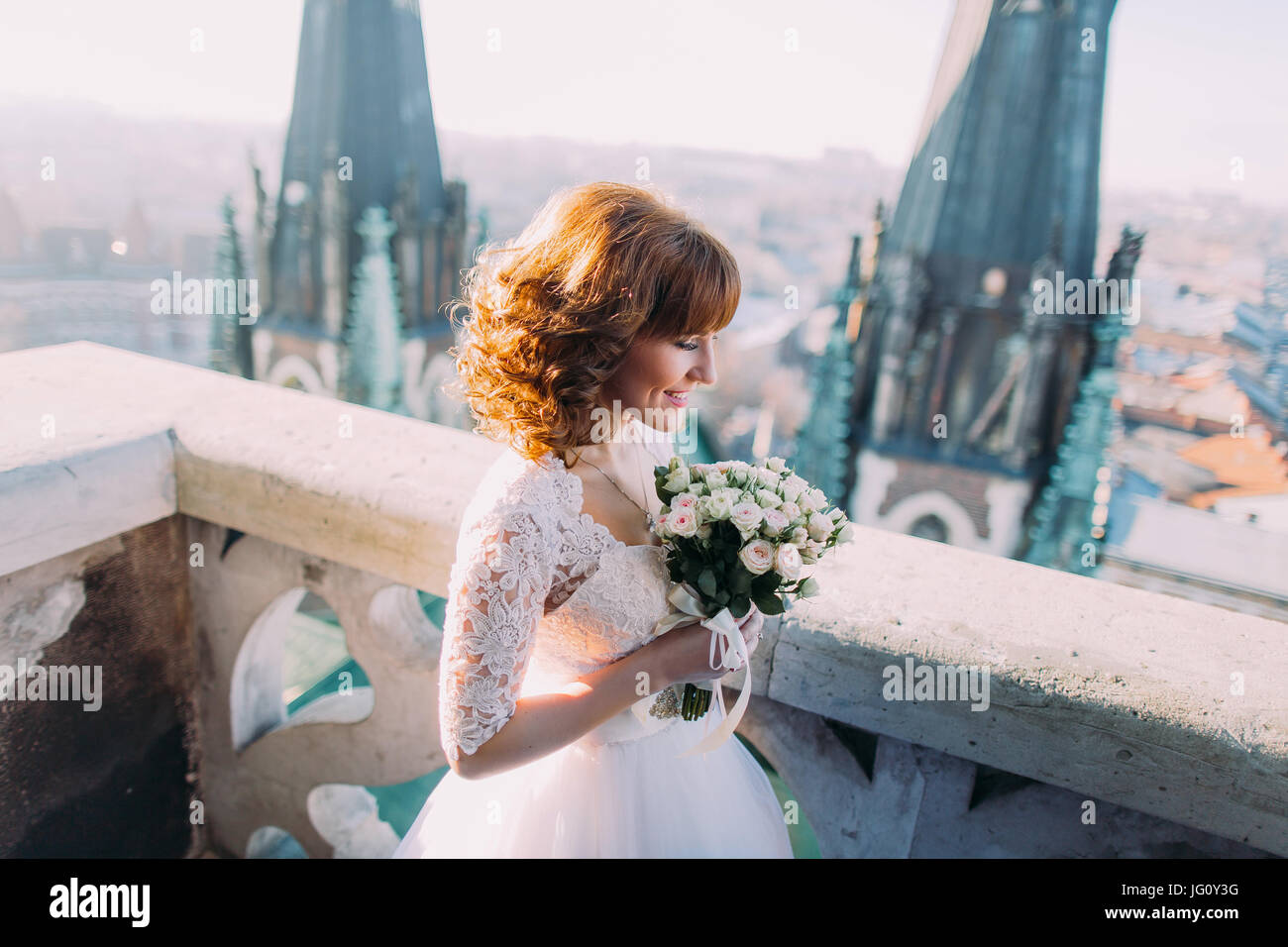 Elegant bride holding rose bouquet on the tower balcony of old gothic ...