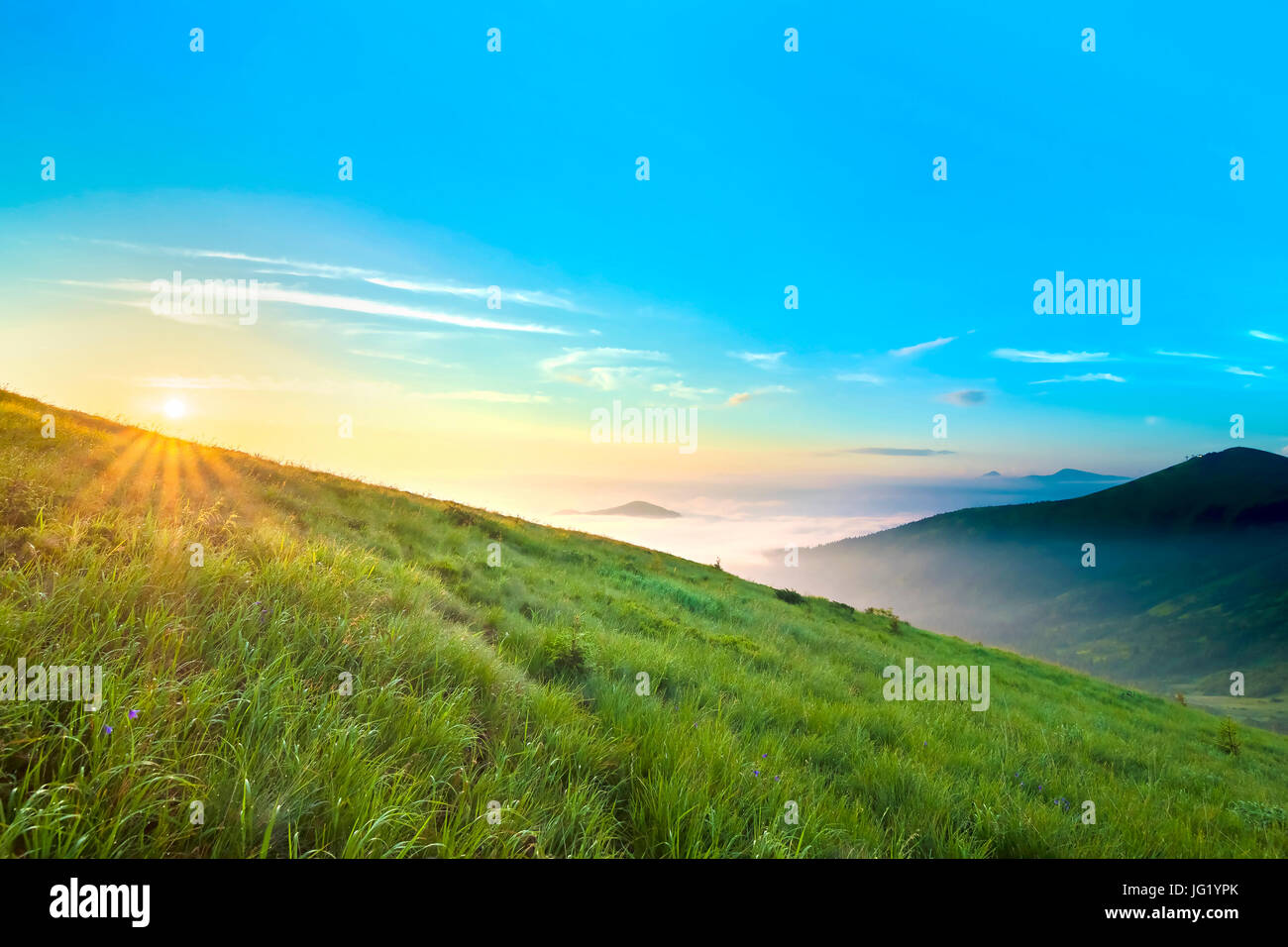 Sunrise over hills in mountains with green grass and blue sky with ...